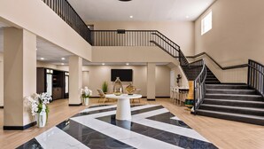 Um hall espaçoso com piso de mármore, uma mesa redonda central, uma escadaria e um candelabro.