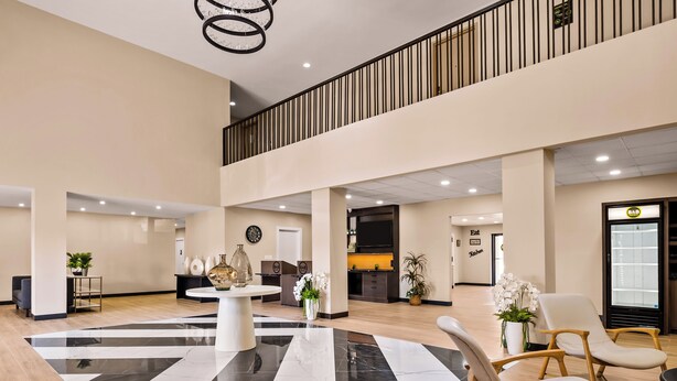 Um hall amplo com piso de mármore preto e branco central, piso de madeira, um candelabro e uma área de estar com cadeiras.