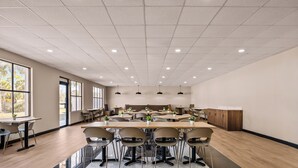 Uma sala de jantar ampla com uma mesa comprida, várias cadeiras, luminárias pendentes e uma cozinha ao fundo.
