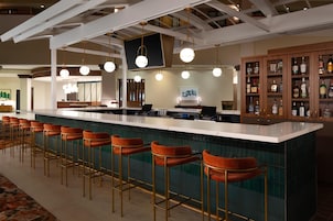 Uma área de bar com um balcão comprido, vários banquinhos e um armário para bebidas.