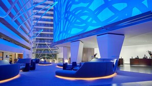 Um lobby moderno de hotel com teto alto, um átrio de vidro e áreas de estar.