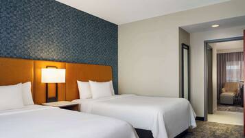 Quarto de hotel com duas camas, cabeceira com luz e vista para outro quarto por uma porta aberta.