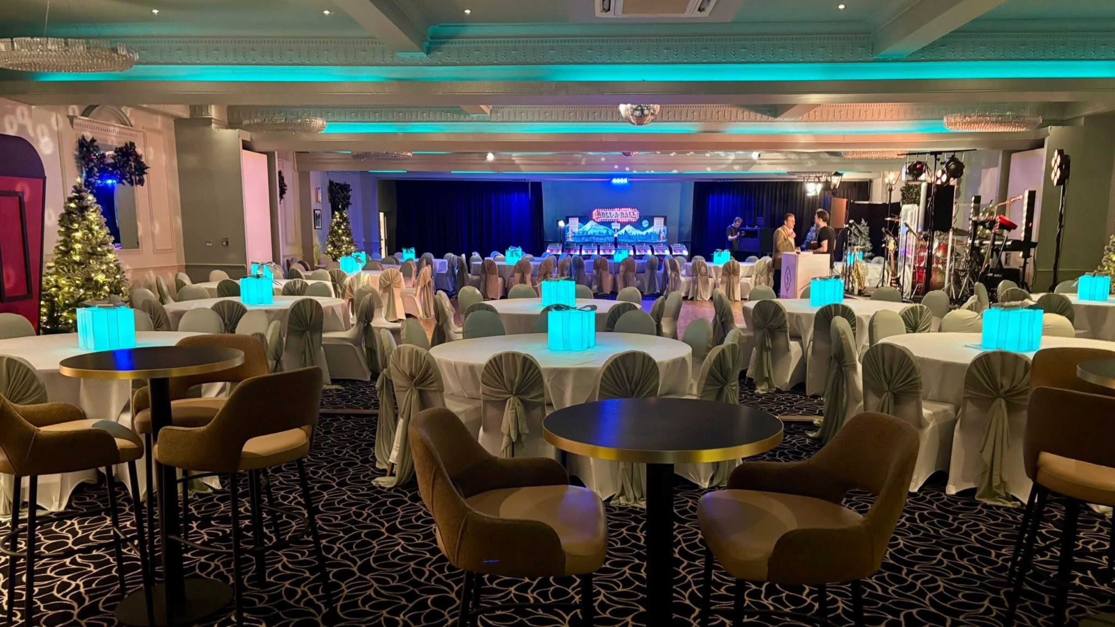 Uma sala de banquetes com mesas redondas, cadeiras e um palco com uma banda.