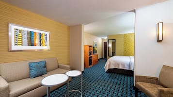 Quarto de hotel com sofá, duas mesinhas, uma cama e um corredor que dá para o banheiro.