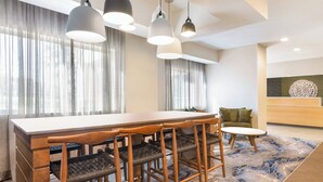 Uma sala de jantar moderna com uma longa mesa de madeira, banquetas e iluminação pendente.