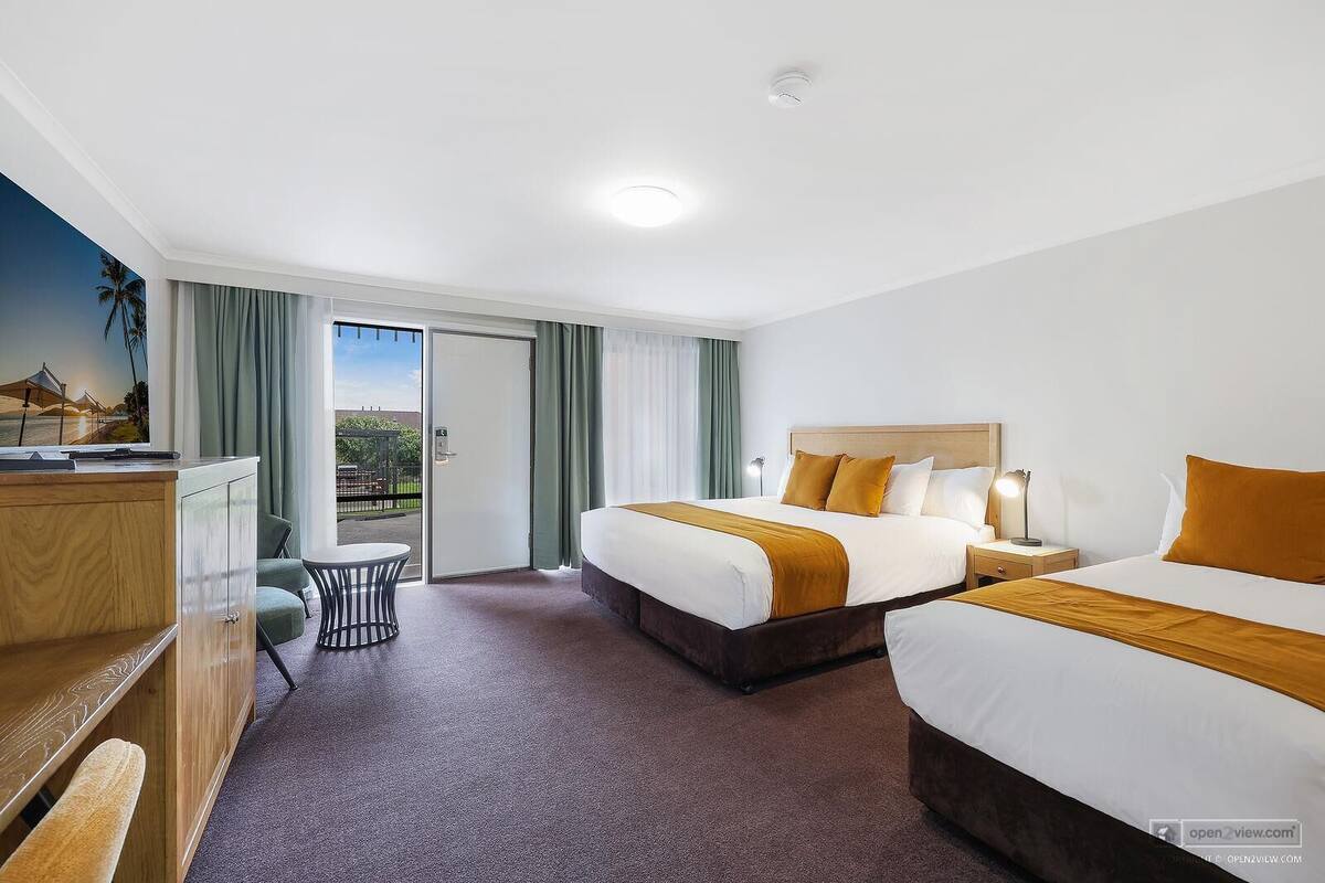 Quarto de hotel com duas camas, uma escrivaninha, uma cadeira e vista para o exterior.