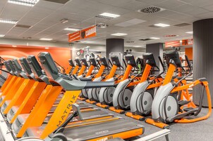 Academia com várias esteiras alinhadas em fileiras, um relógio e uma placa indicando área de cardio.