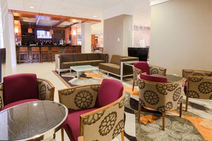 Um saguão de hotel com áreas de estar, um bar e uma televisão.