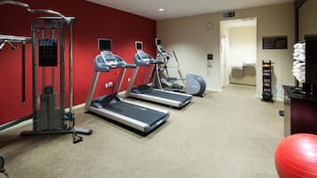 Academia com esteiras, uma máquina de pesos e uma bola de exercício vermelha.