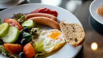 Mesa de café da manhã com pratos de comida, incluindo ovos, linguiça e torradas, além de xícaras de café e um copo de suco de laranja.