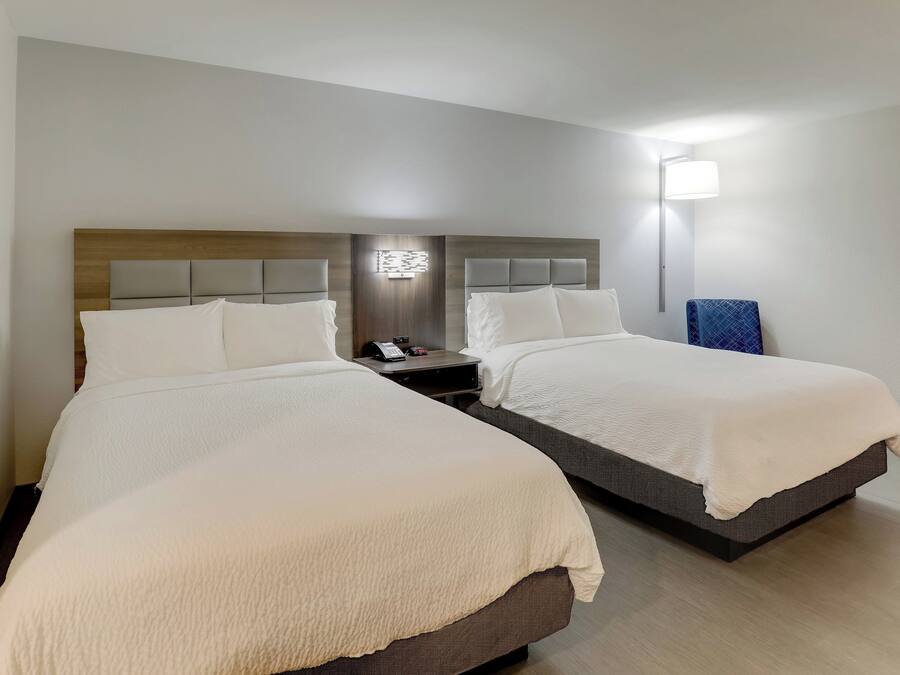 Quarto de hotel com duas camas, uma mesa de cabeceira, uma luminária na parede e um quadro emoldurado.