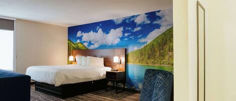 Quarto de hotel com cama, escrivaninha, cadeira e um grande mural de paisagem montanhosa.