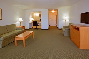 Quarto de hotel com sofá, mesa pequena, televisão e escrivaninha com cadeira.