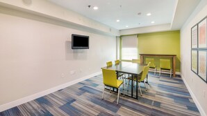 Sala de conferências com mesa, cadeiras, TV de tela plana na parede e janela com persianas.