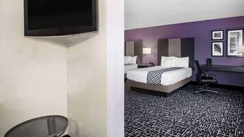 Quarto de hotel com cama, escrivaninha, cadeira e televisão na parede.