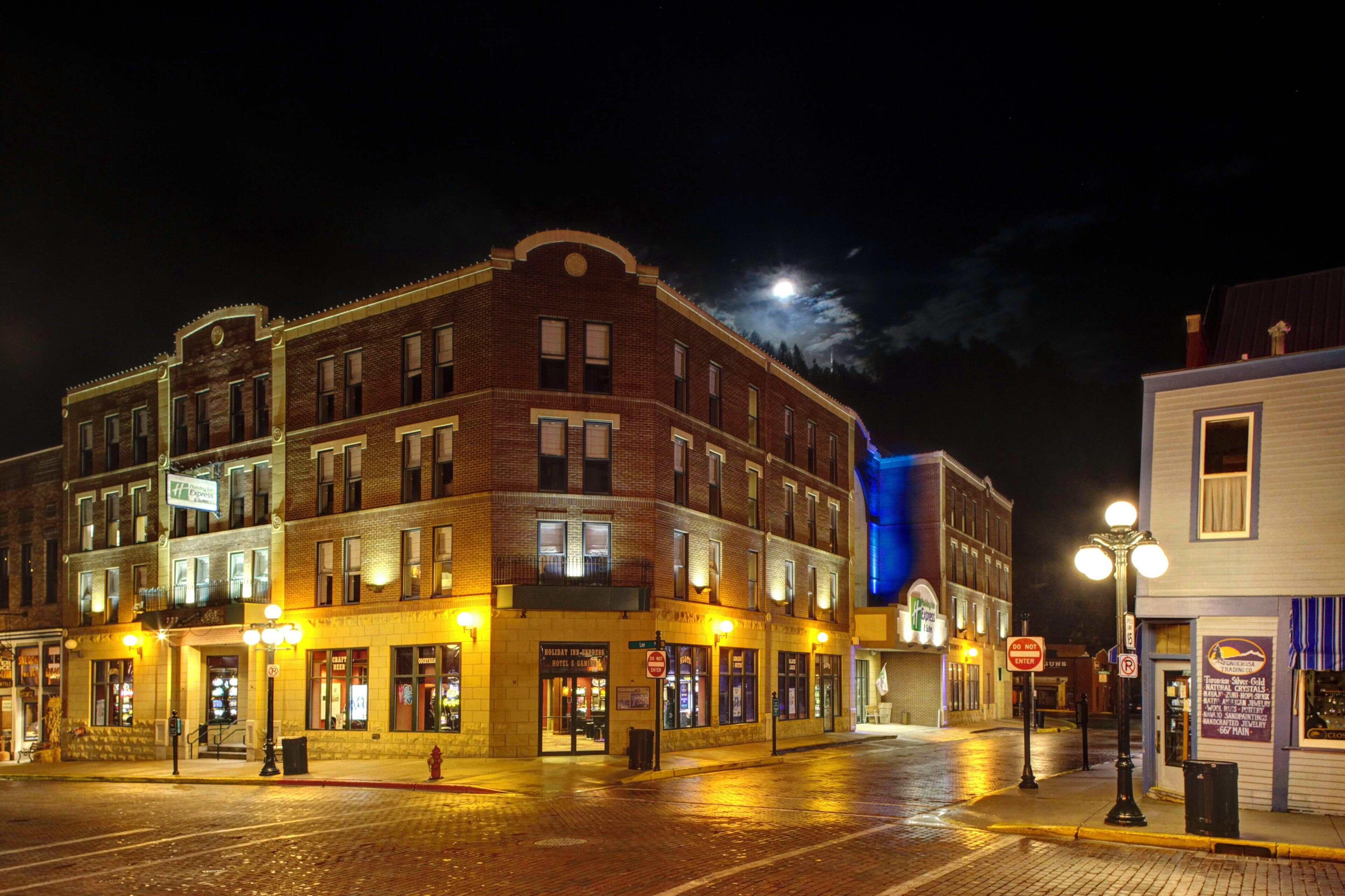 Um edifício histórico com vários andares, com entrada na esquina e letreiros iluminados.