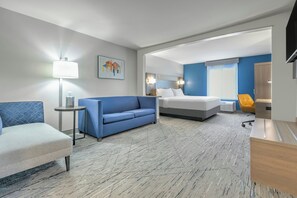 Quarto de hotel com uma cama, um sofá azul, uma mesinha, um abajur e um quadro na parede.