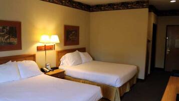 Quarto de hotel com duas camas de solteiro, uma mesinha de cabeceira com abajur e uma escrivaninha de madeira.