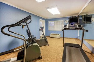 Uma sala de ginástica com equipamentos de exercício, esteira e espelho.
