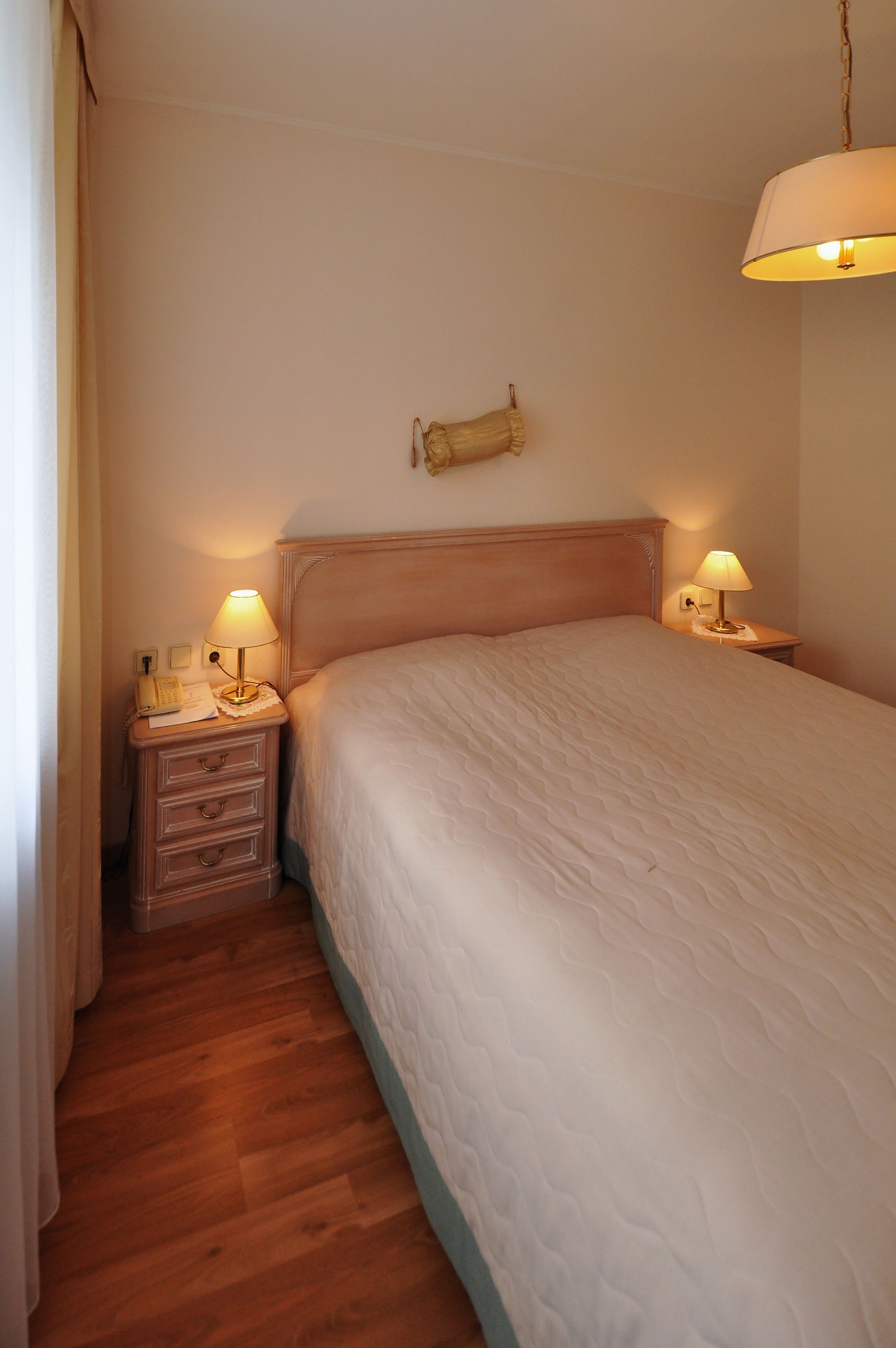 Quarto com cabeceira de madeira, mesa de cabeceira com abajur e criado-mudo com telefone.