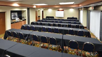 Uma sala de conferência com mesas e cadeiras dispostas em fileiras, uma tela de projeção e um pódio.
