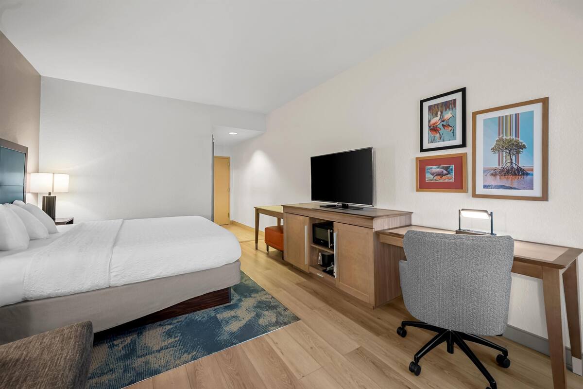 Quarto de hotel com cama, escrivaninha, televisão e obras de arte na parede.