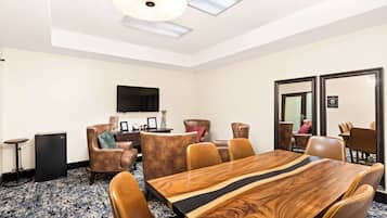 Uma sala de conferências com uma grande mesa de madeira, cadeiras de couro, uma TV de tela plana e piso coberto de carpete.