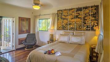 Quarto de hotel com uma cama grande, uma cadeira, uma janela, uma parede com obras de arte e uma porta que dá para uma varanda.