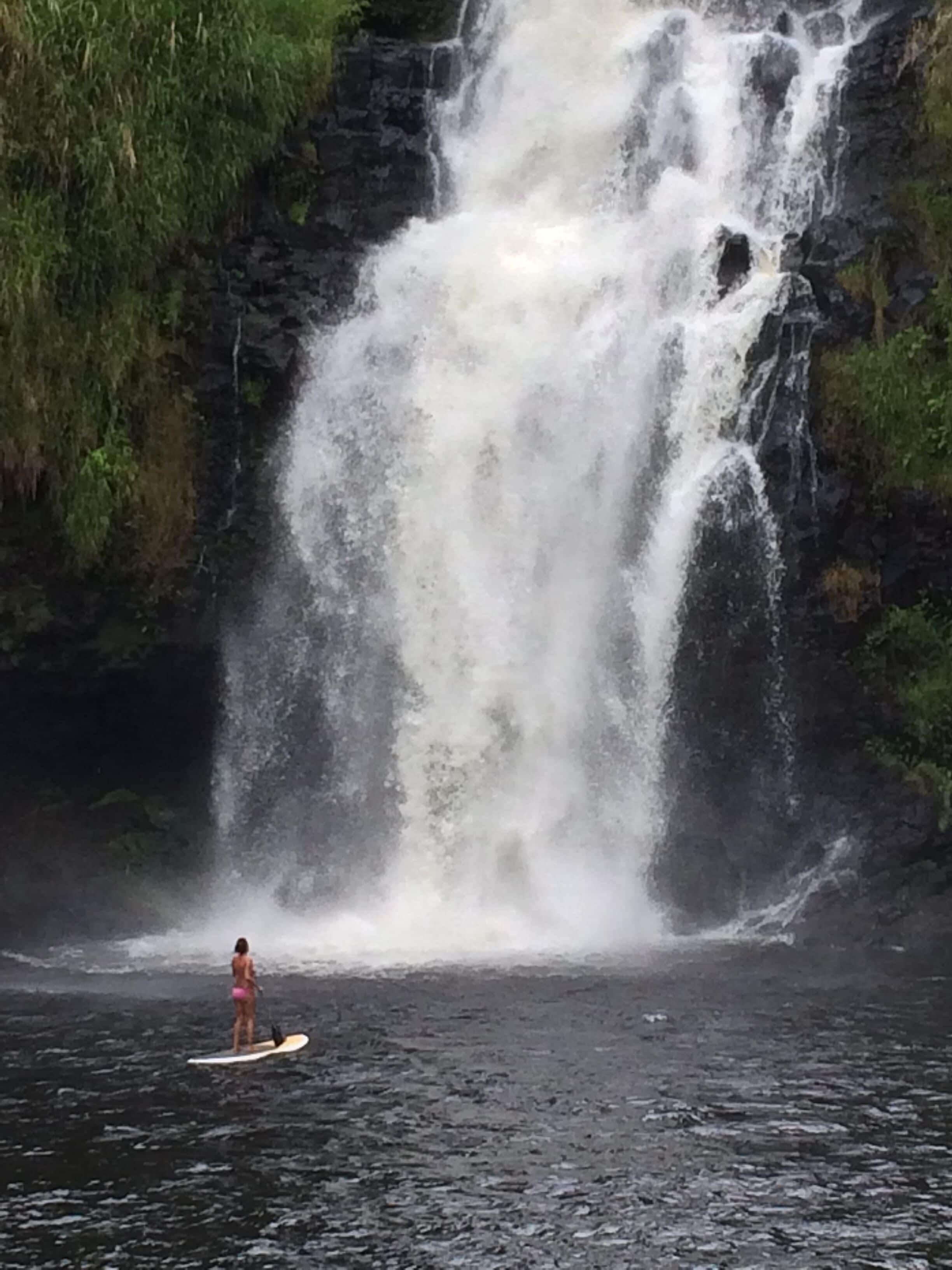 Uma pessoa em pé em uma prancha de surf em frente a uma cachoeira.