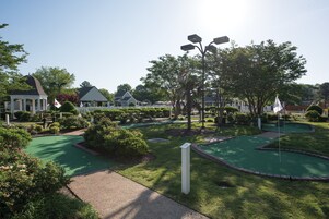 Um campo de mini golfe com um coreto, árvores e céu limpo.