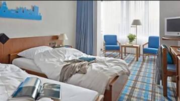 Quarto de hotel com duas camas, uma televisão, uma secretária com cadeira e uma mesinha de cabeceira com abajur.