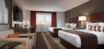 Quarto de hotel com duas camas, um sofá, uma TV, uma escrivaninha e uma janela com cortinas.