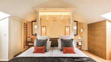 Quarto moderno com uma cama grande, um guarda-roupa de madeira e um banheiro visível por uma porta aberta.