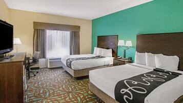 Quarto de hotel com duas camas, uma escrivaninha, televisão e uma janela com cortinas.