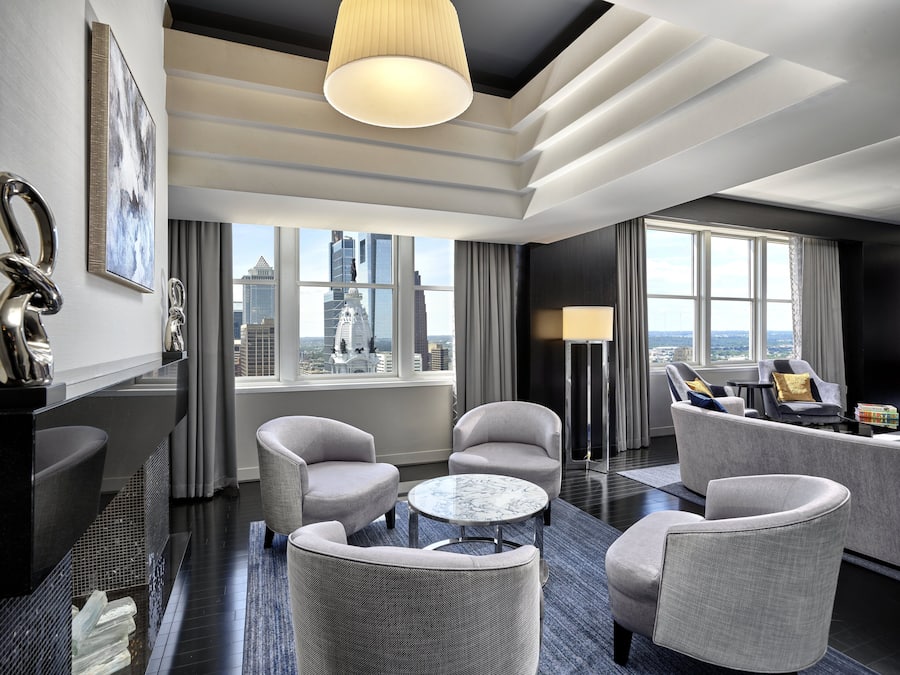 Quarto de hotel moderno com vista para a cidade, um sofá, uma mesa redonda e uma janela grande.