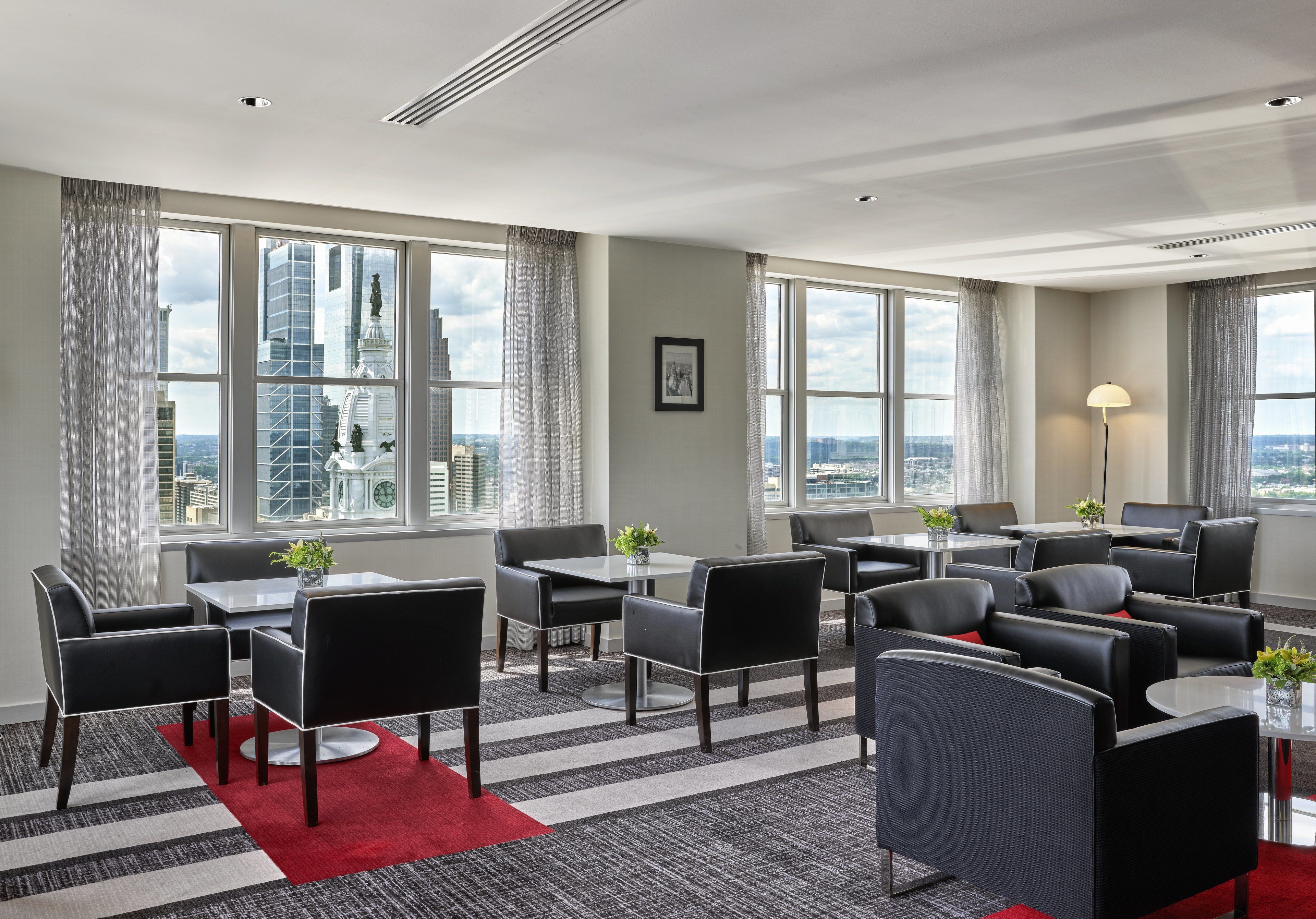 Quarto de hotel com grandes janelas, área de refeições e diversas opções de assento.