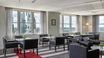 Quarto de hotel com grandes janelas, área de refeições e diversas opções de assento.