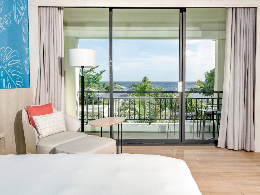Quarto de hotel com uma cama grande, um sofá, uma mesinha e uma varanda com vista para o mar.