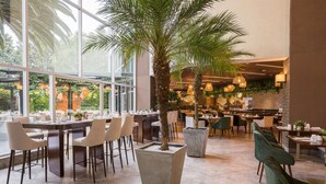 Um restaurante espaçoso com tetos altos, janelas amplas e diversos arranjos de assentos, incluindo mesas e cadeiras.