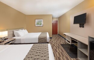 Quarto de hotel com duas camas, uma escrivaninha, uma cadeira, uma televisão e uma porta.