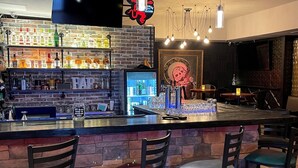Uma área de bar com balcão de pedra, vários bancos altos, uma geladeira com bebidas e luminárias pendentes.