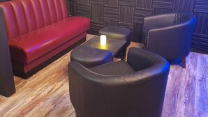 Quarto com sofá vermelho, duas poltronas pretas, uma mesa pequena com uma vela e parede estampada.