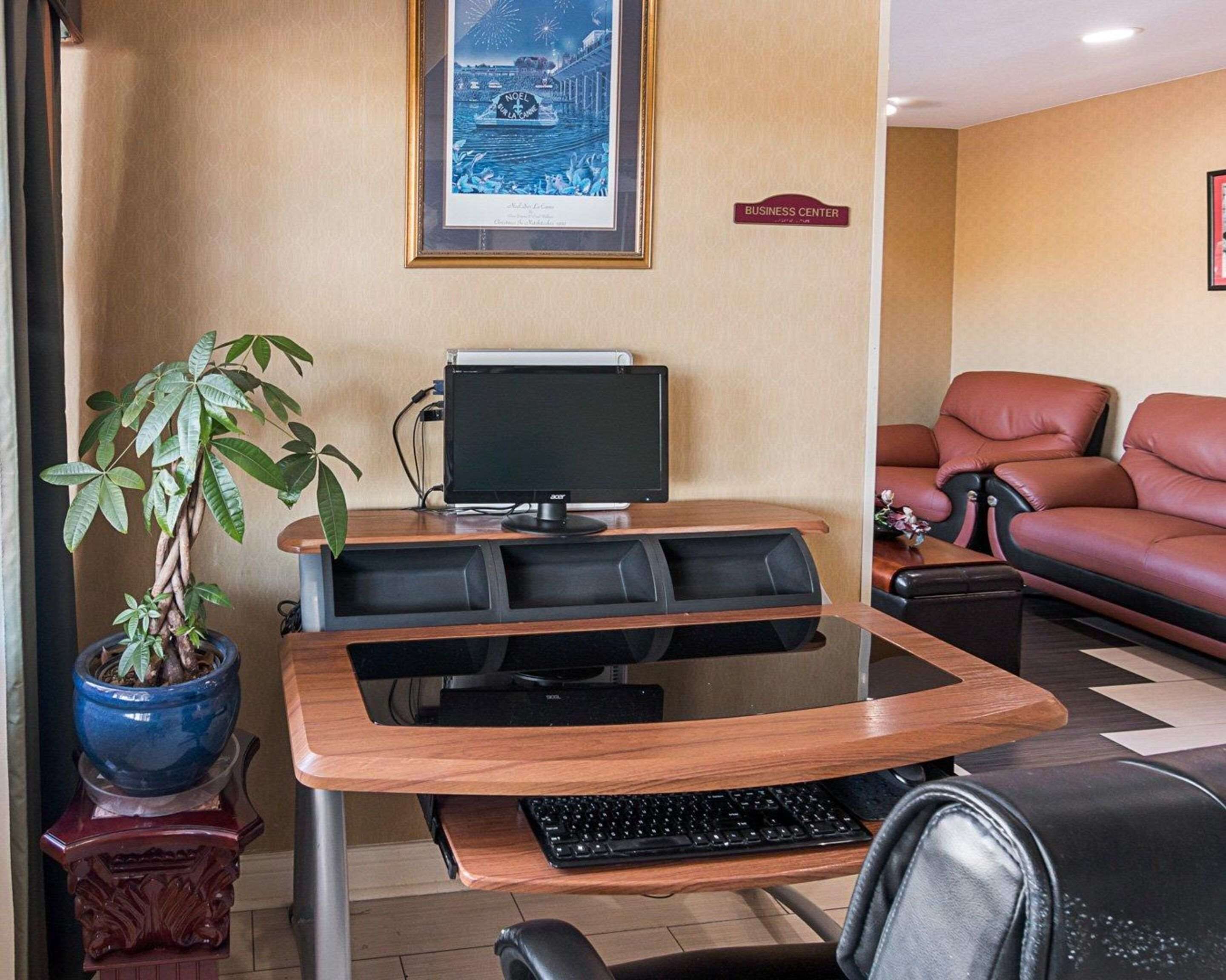 Quarto de hotel com escrivaninha, computador e dois sofás de couro.