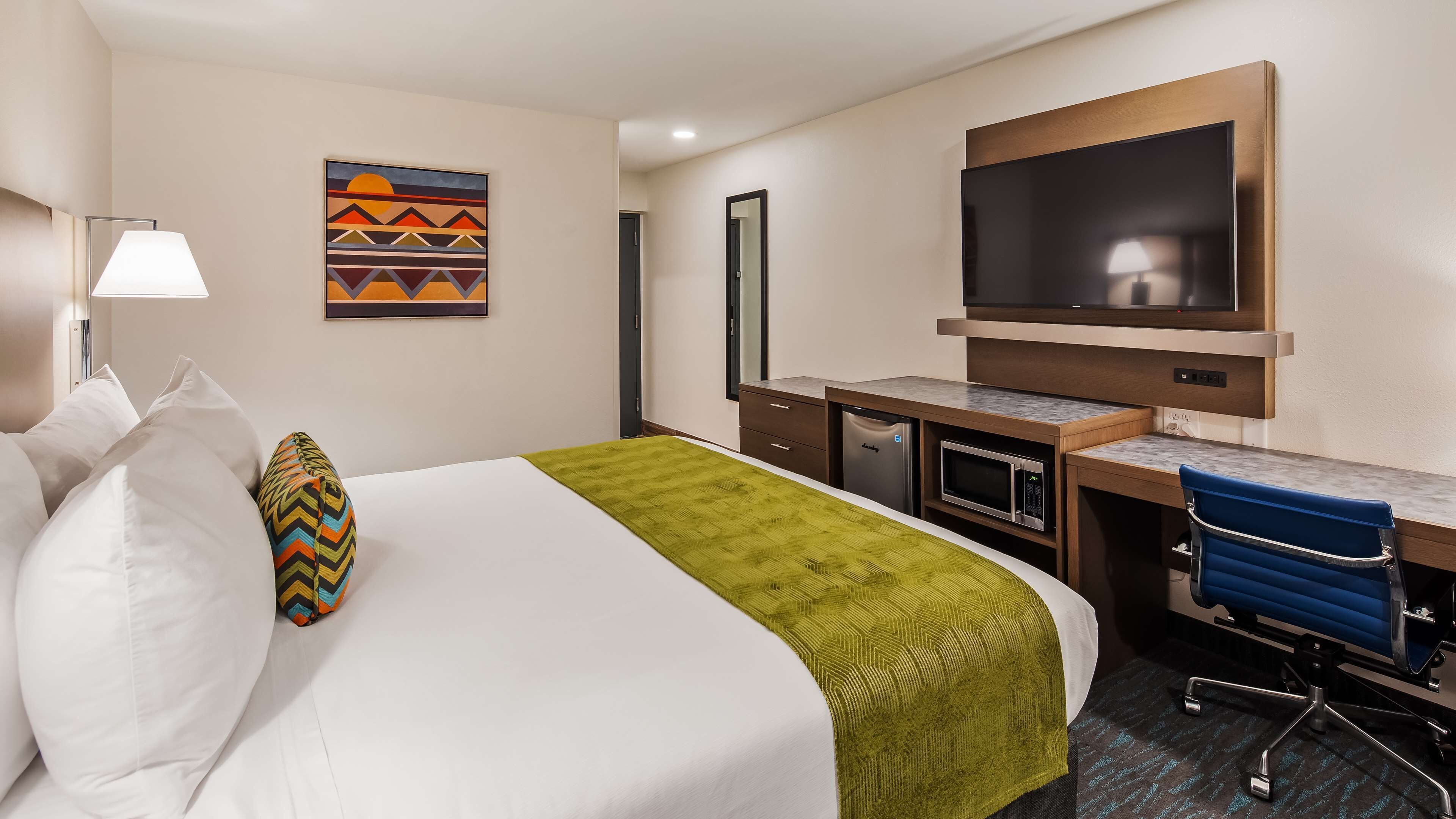 Quarto de hotel com cama, escrivaninha, televisão e micro-ondas.
