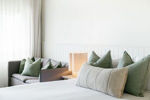 Quarto de hotel com cama, cadeira, luminária e janela com cortinas.