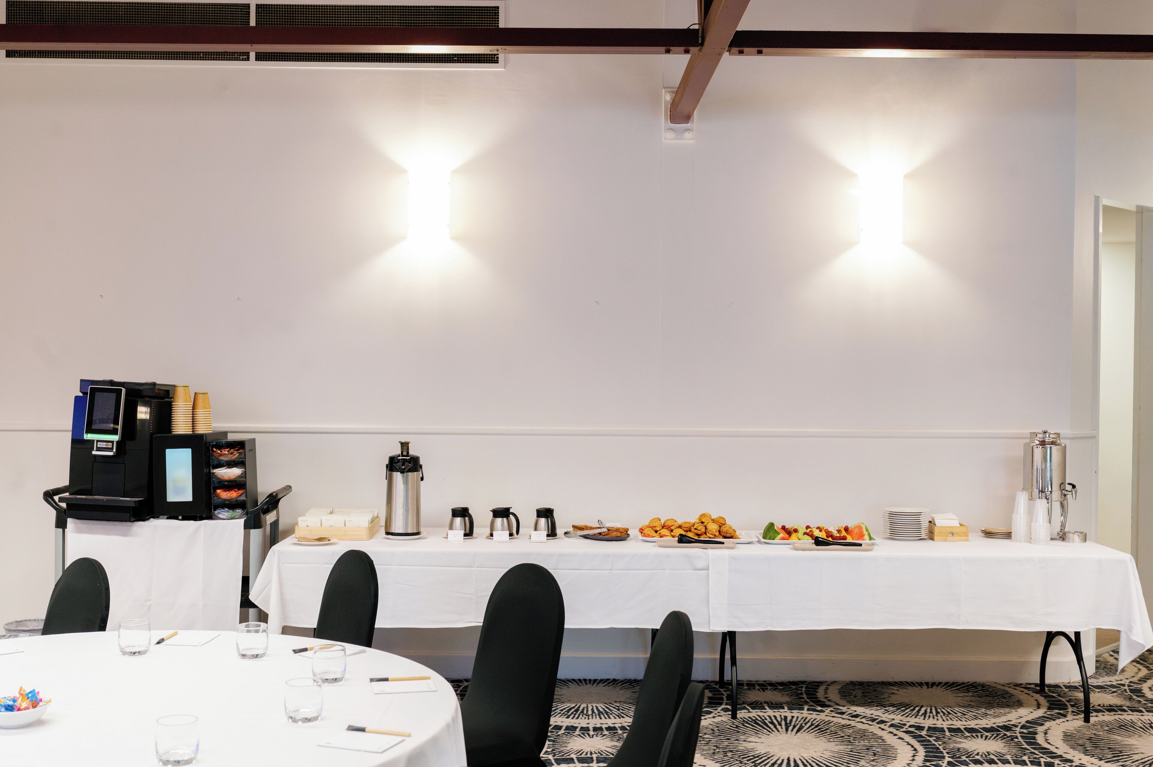 Uma sala de conferências com uma mesa branca, cadeiras pretas, um canto para café e um buffet.