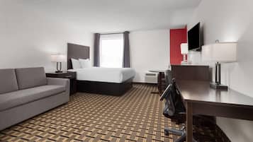 Quarto de hotel com cama, sofá, escrivaninha, televisão e janela com cortinas.