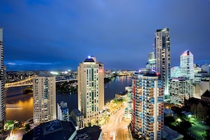 Vista noturna de uma cidade com edifícios altos, um rio e uma ponte.