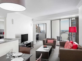 Quarto de hotel moderno com área de jantar, TV, sofá e vista para a cidade.