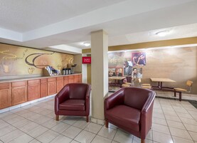 Um saguão de hotel com balcão de recepção, duas poltronas de couro, uma máquina de café e uma parede com um letreiro de boas-vindas.